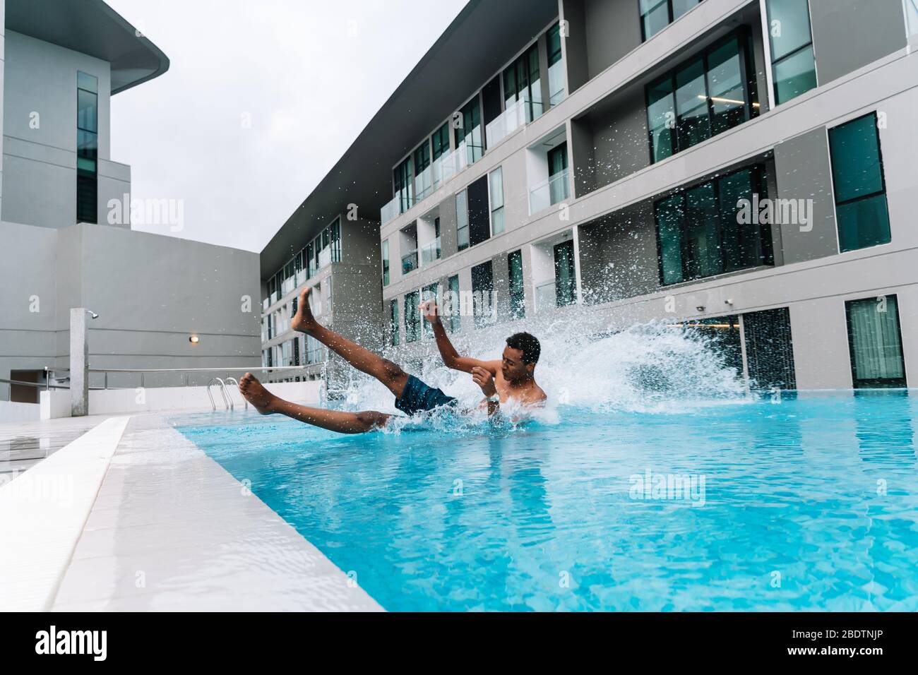 Young boy jumping and falling into a pool surrounded by modern ...