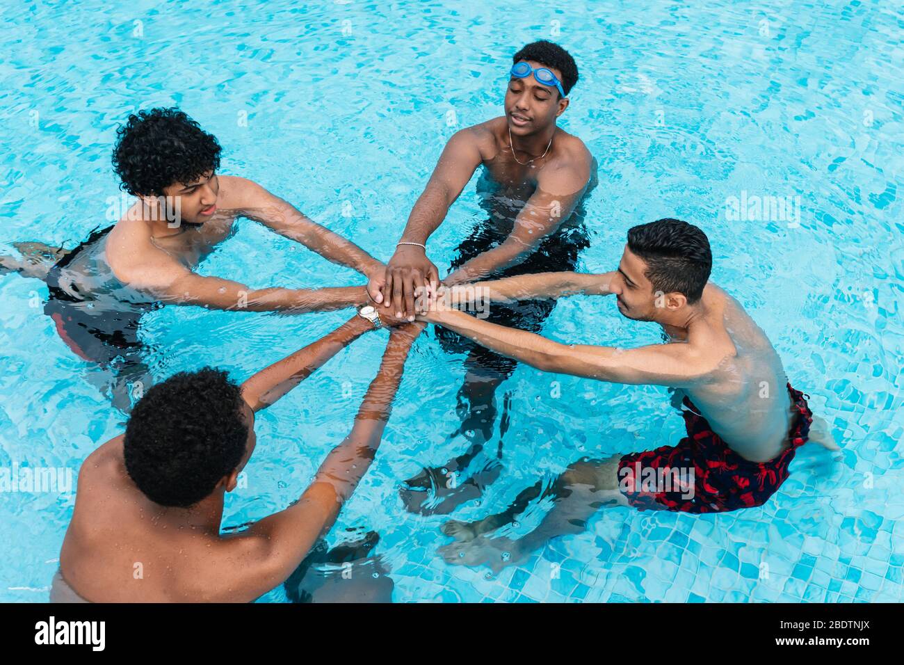 Group of young people gathering their hands in a circle inside a pool ...