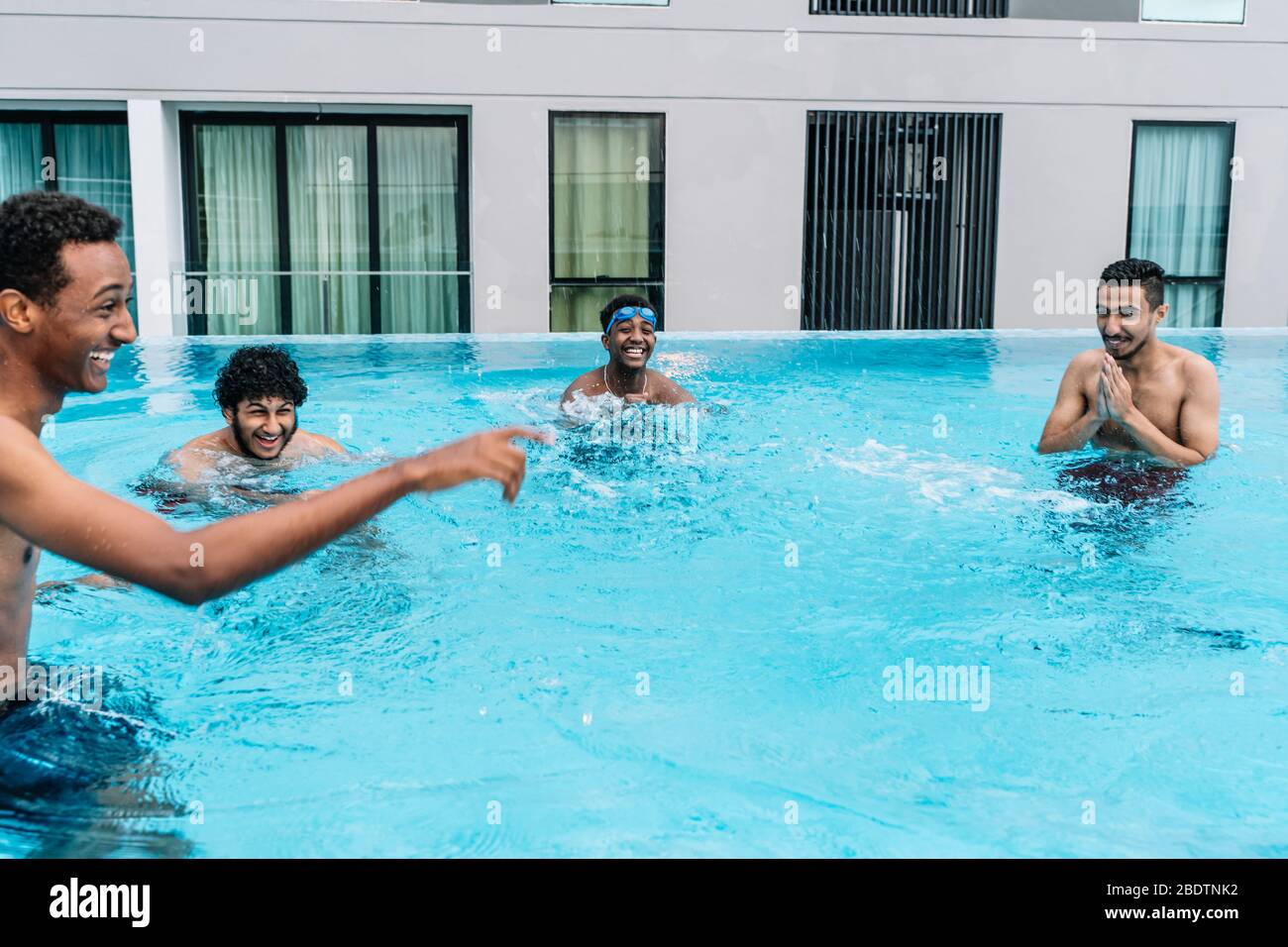 Group of young people making jokes inside a pool surrounded by ...