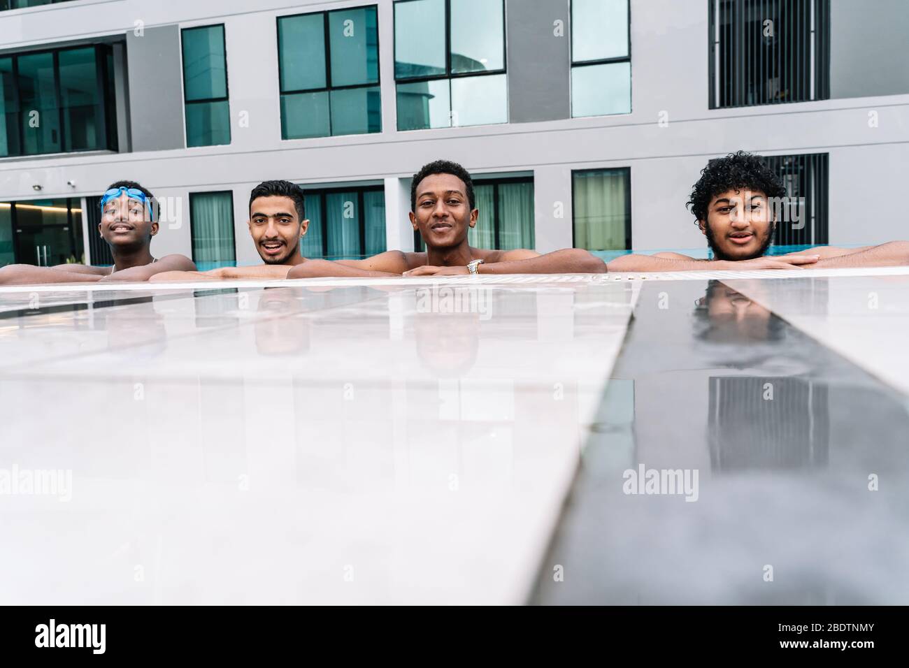 Group of young people leaning on the edge of a pool surrounded by ...