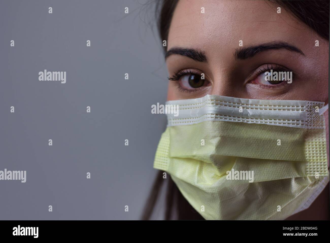 Female hospital worker wearing yellow face mask. Eyes visible over ...