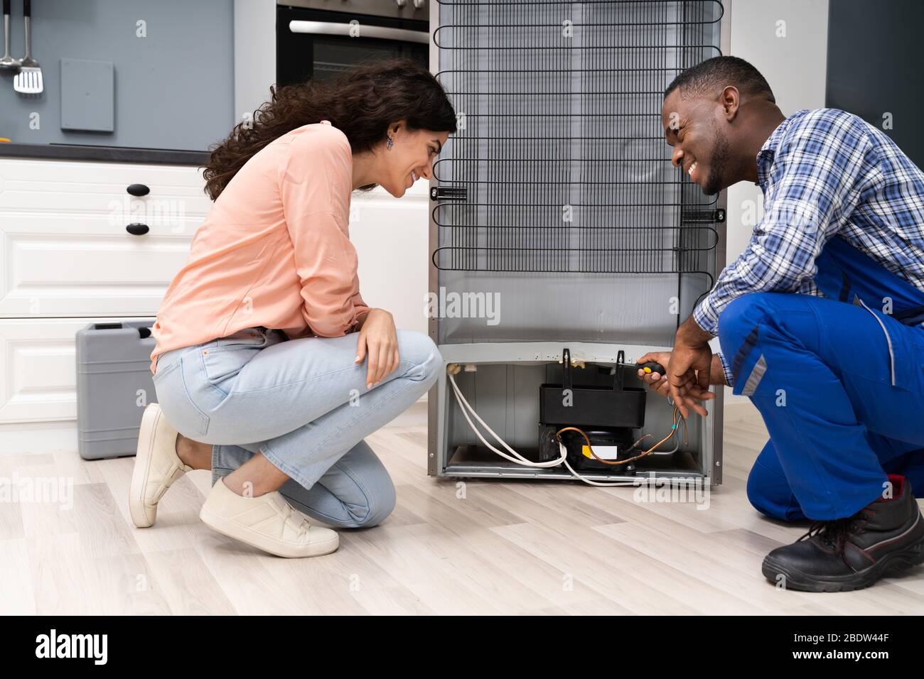 Young Repairman Repairing Refrigerator In Front Of Beautiful Woman ...