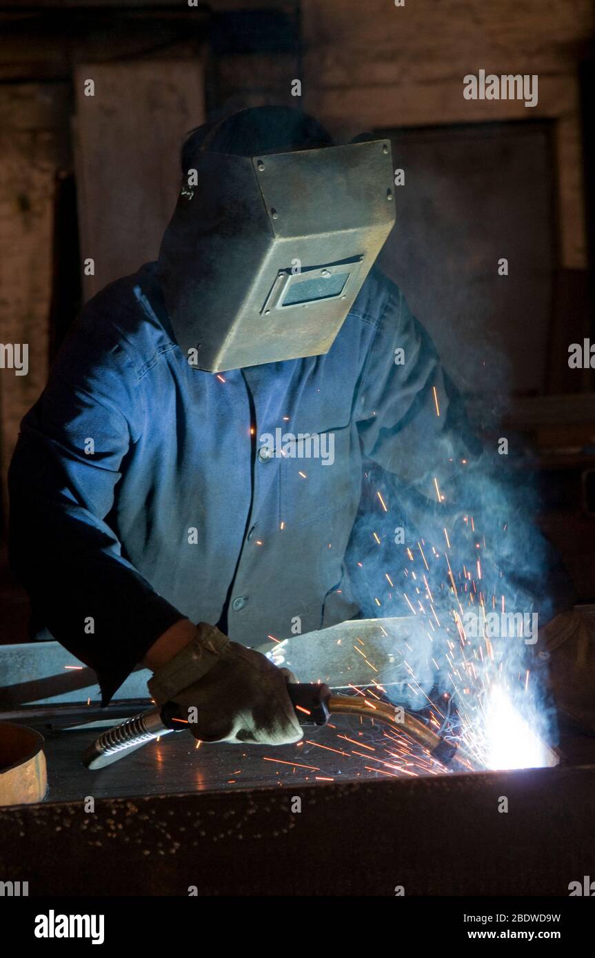 Working man with helmet shield on his head is welding steel ...