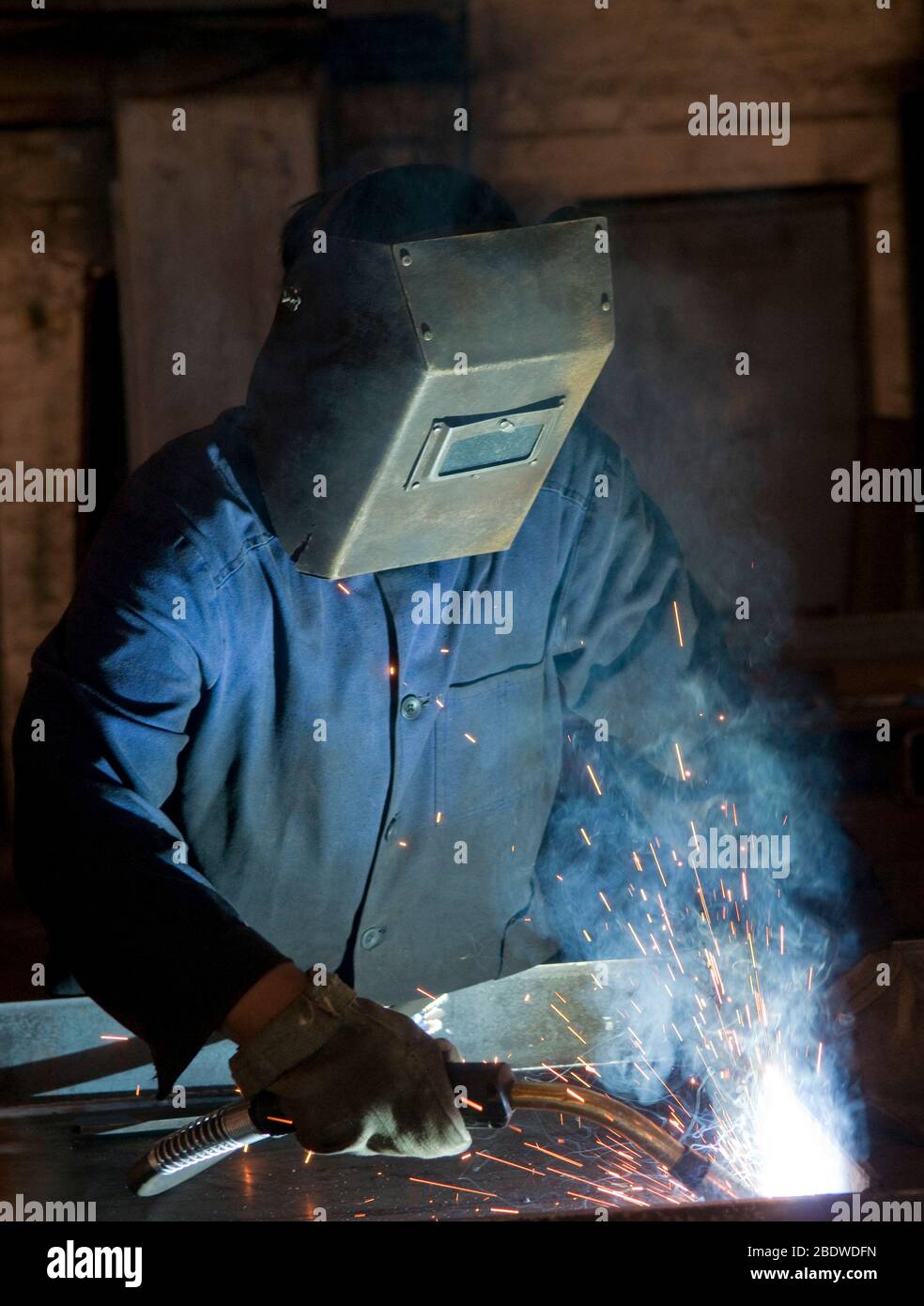 Working man with helmet shield on his head is welding steel ...