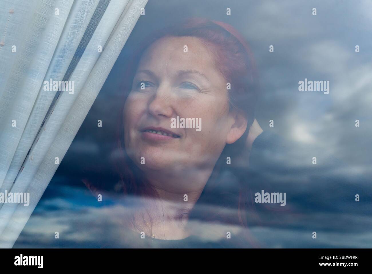 Woman looking through the window on a rainy day with blurred clouds ...