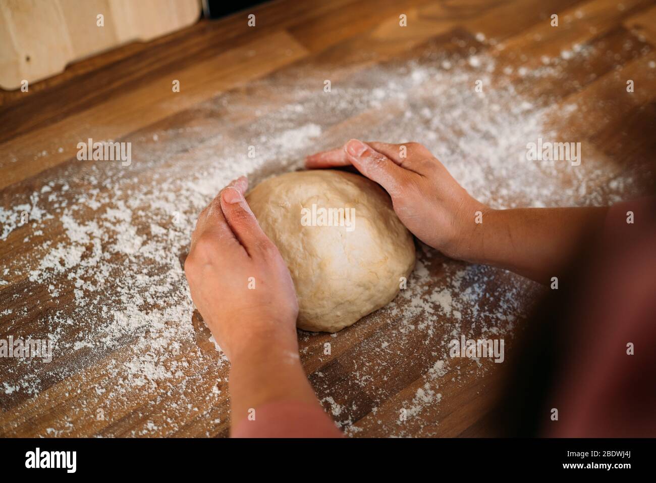 Woman's hands with a ball of dough on the wooden counter to knead it to ...