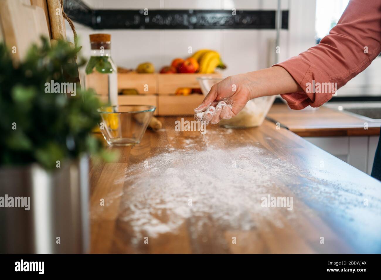 Woman putting flour on wooden kitchen counter to knead pizza dough ...