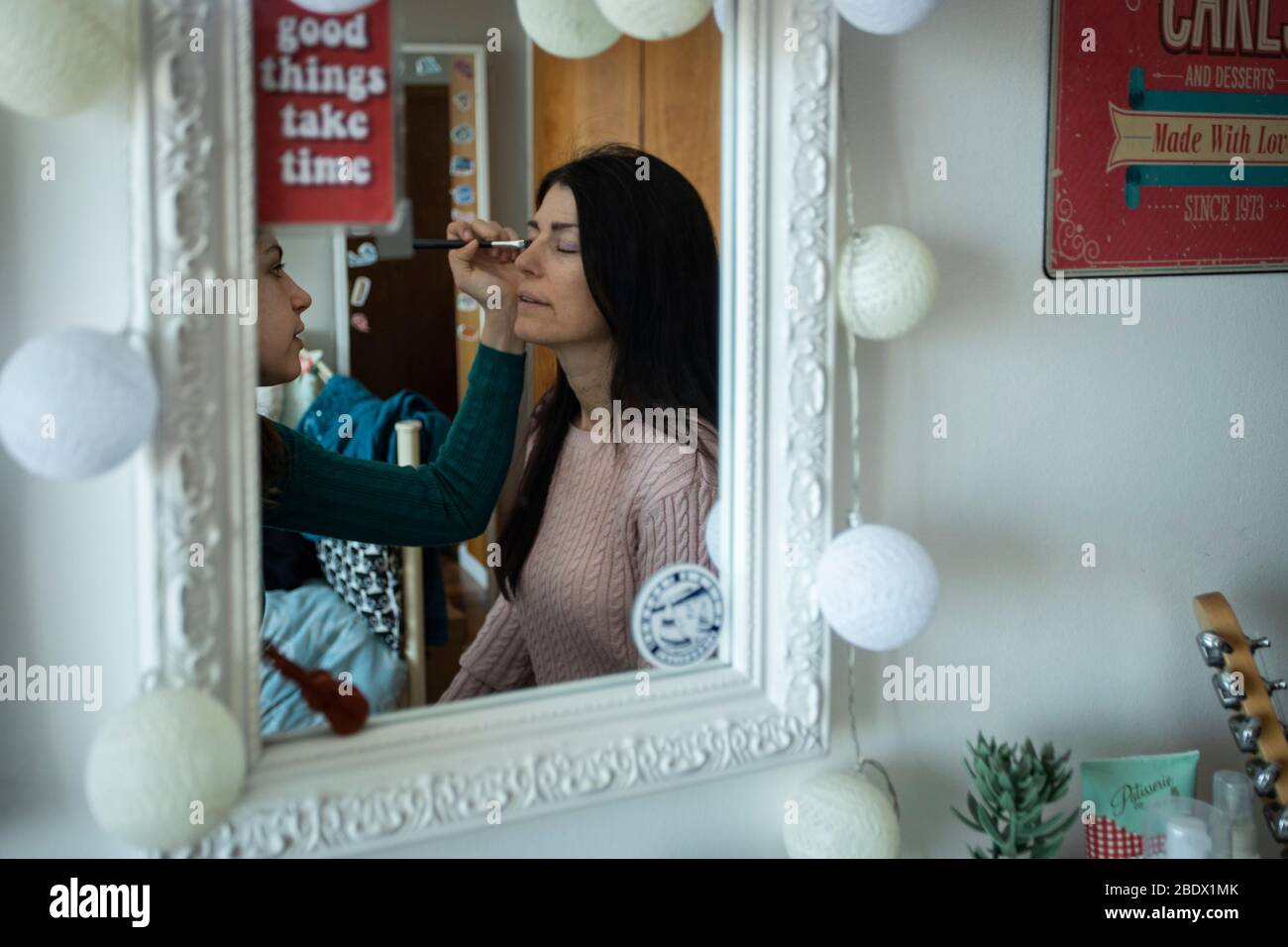 Teenage girl putting make-up on her mother at home during Covid19 ...