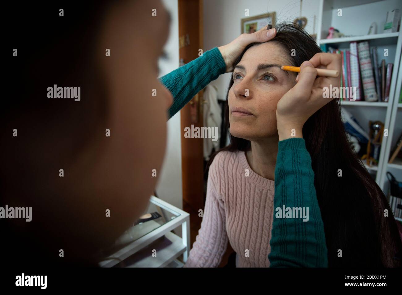 Teenage girl putting make-up on her mother at home during Covid19 ...