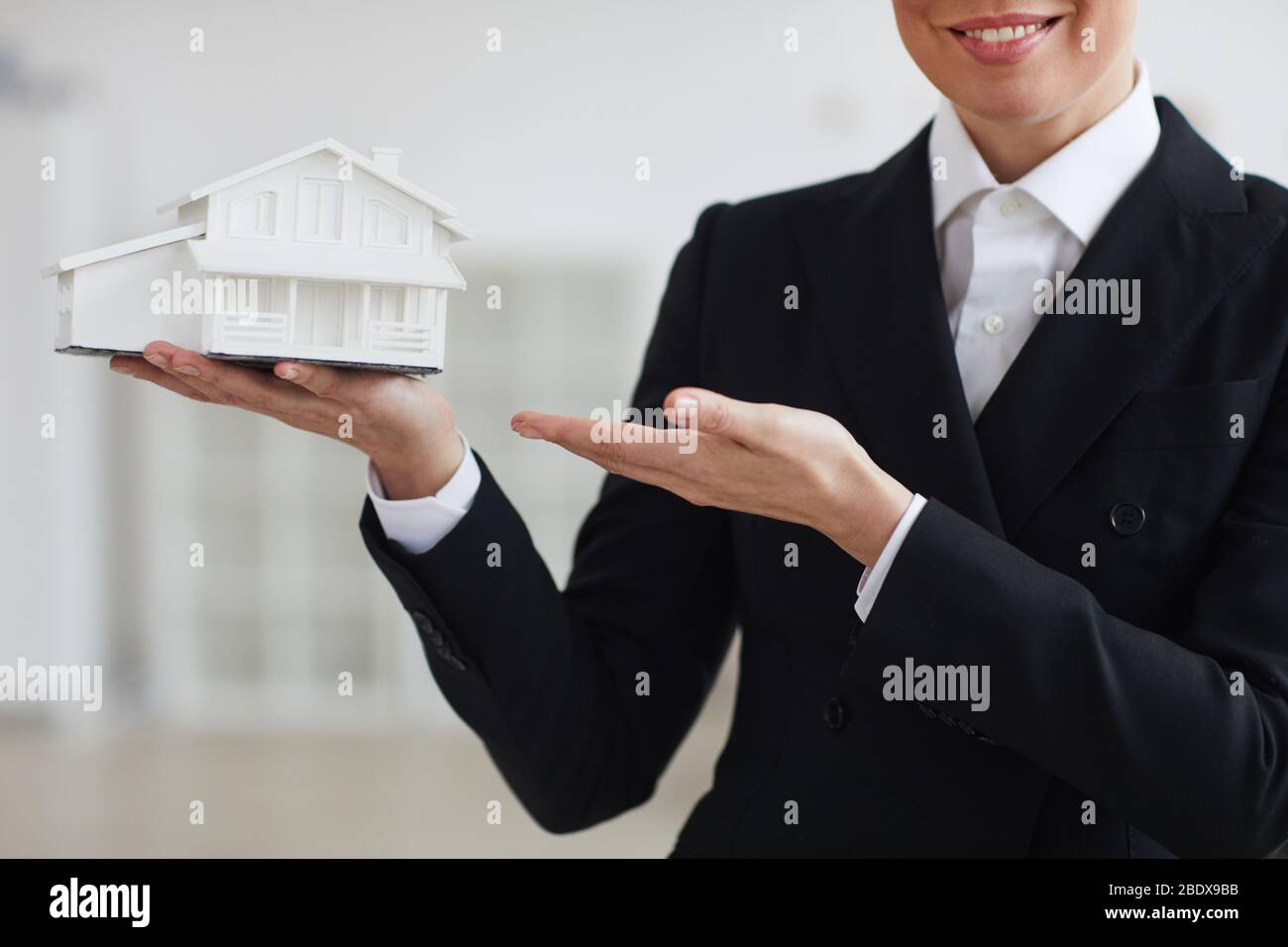 Close-up of realtor in black suit holding model of the house and ...