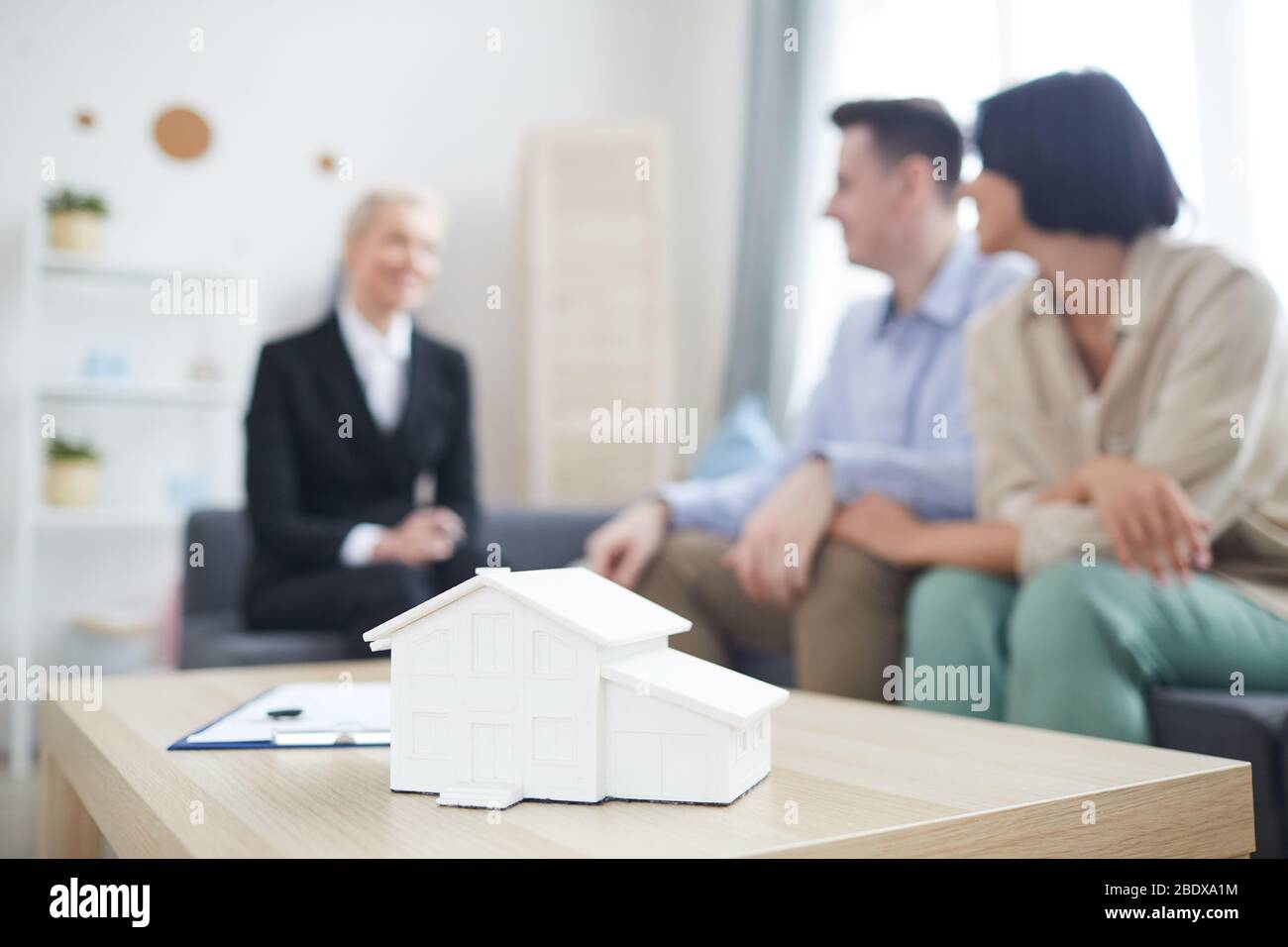 Close-up of model of new house on the table with young couple and real ...