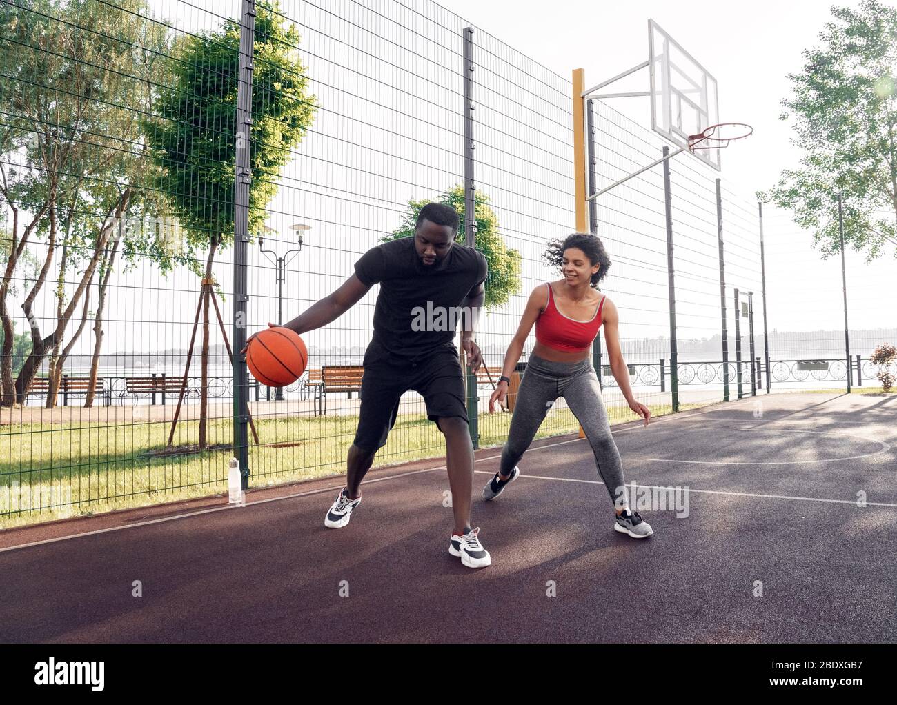 Outdoors Activity. African couple on basketball court guy dribbling ...
