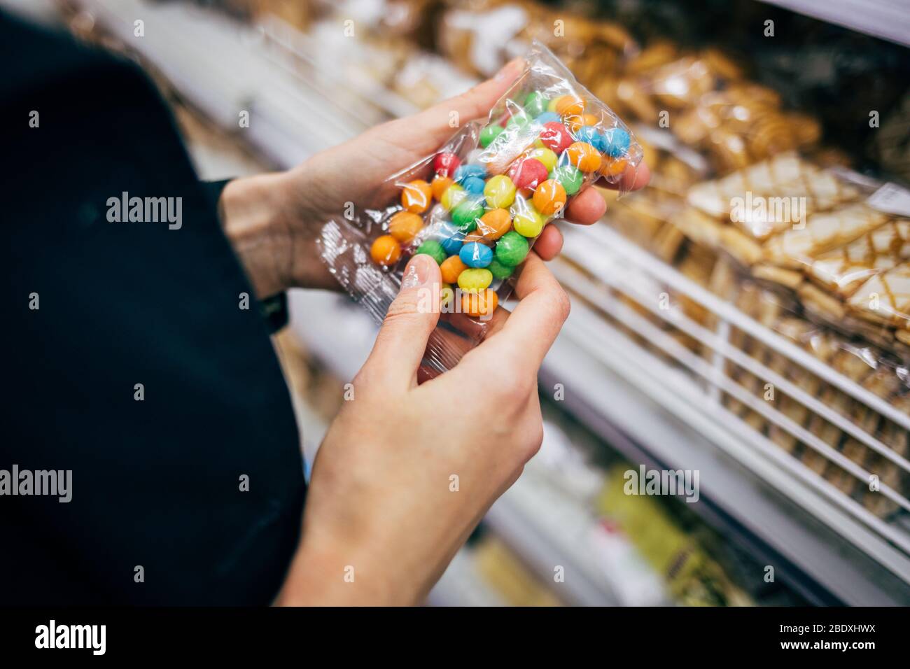 Female hands holding package of candies near shelf in confectionery ...