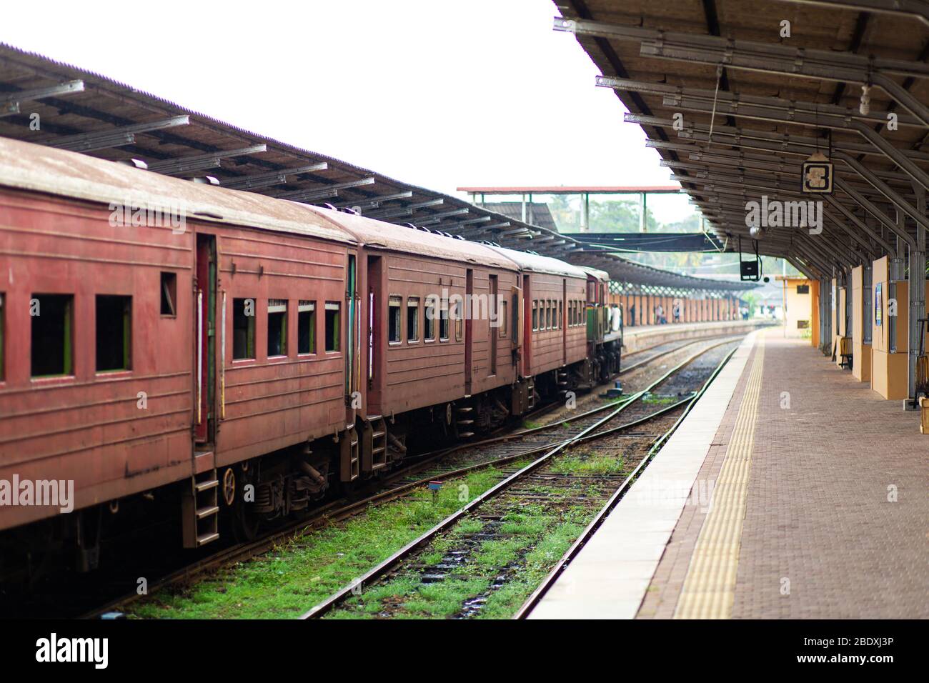 Empty platform of a railway station in Sri Lanka. Old rusty train cars ...