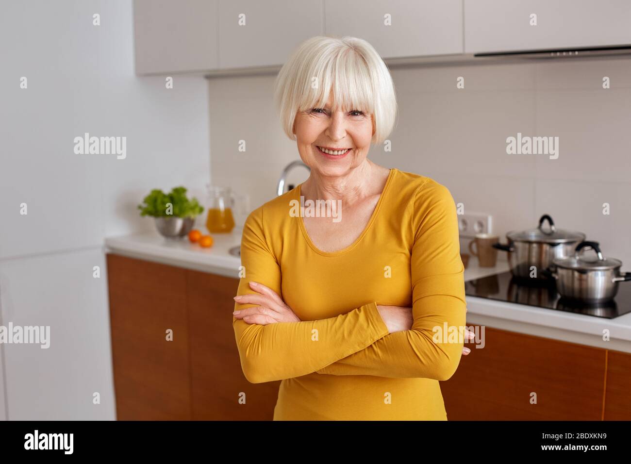 Retirement. Senior woman standing at kitchen crossed arms smiling happy ...