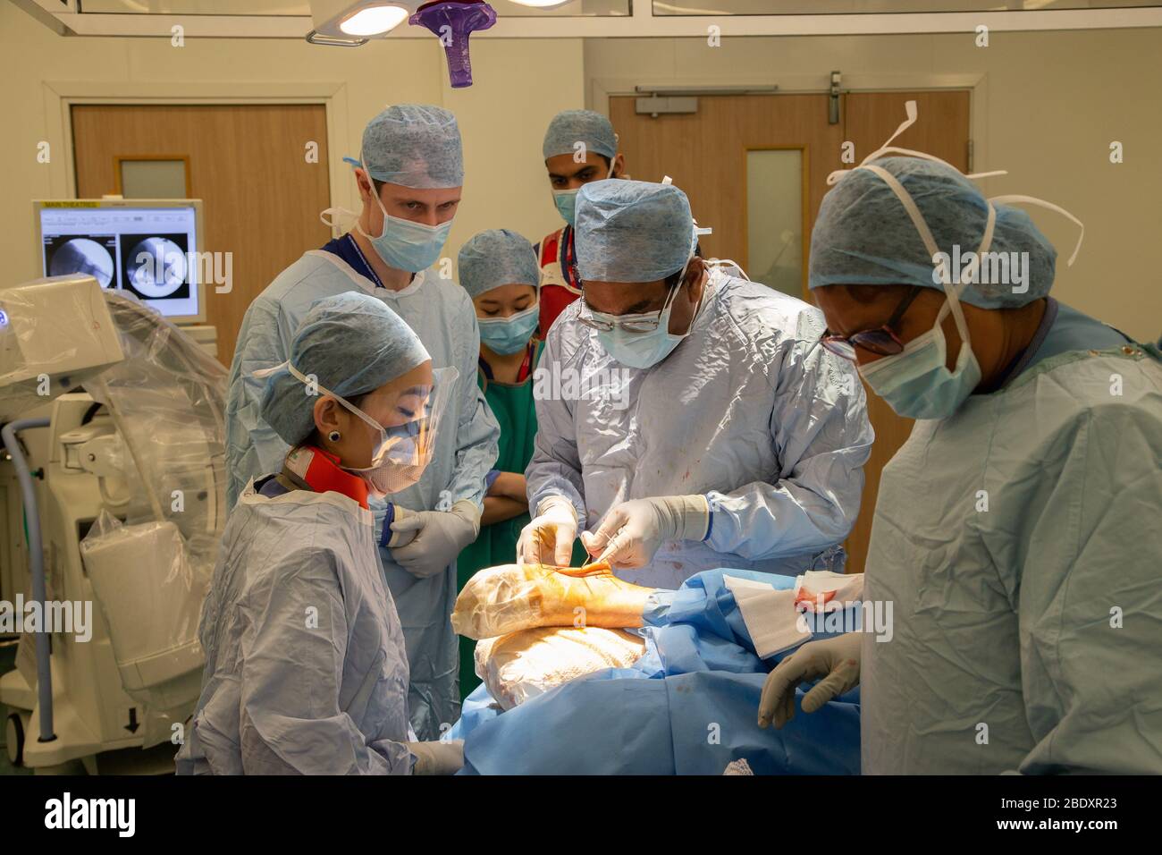 Surgeons and technicians insert a metal plate into the ankle area of a ...