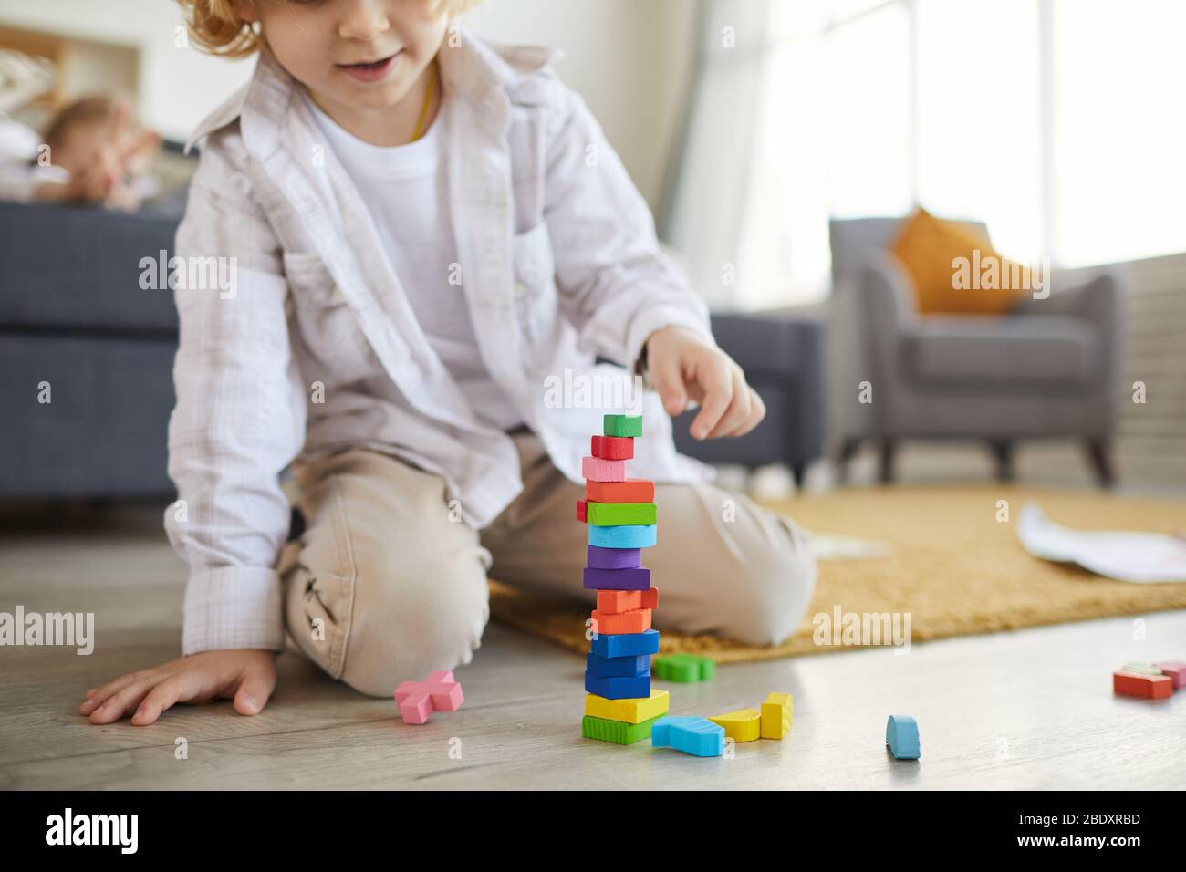 Close-up of little boy sitting on the floor and building a tower from ...