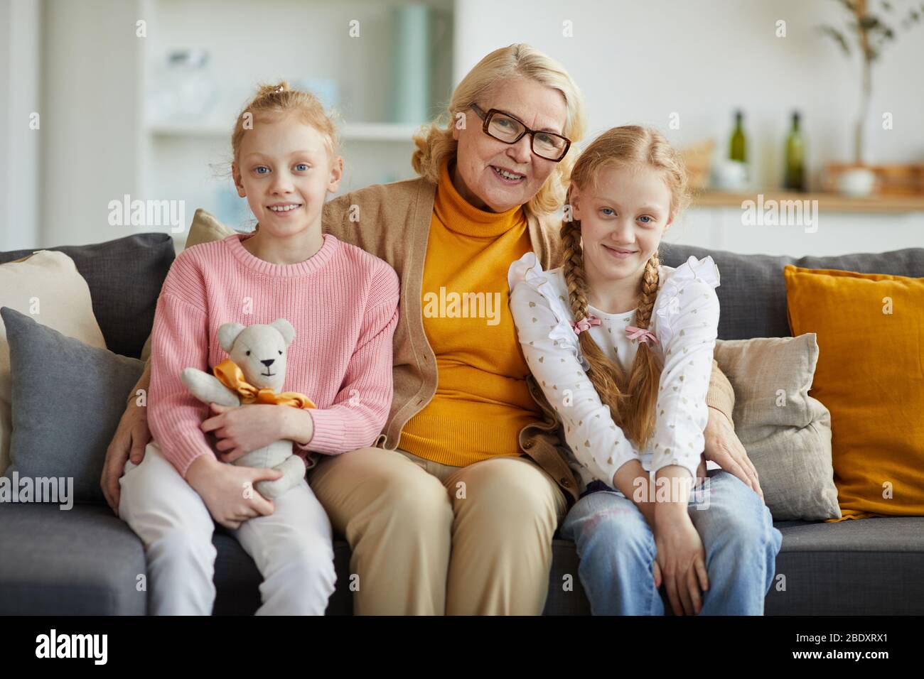 Portrait of happy grandmother sitting on the sofa and embracing her two ...