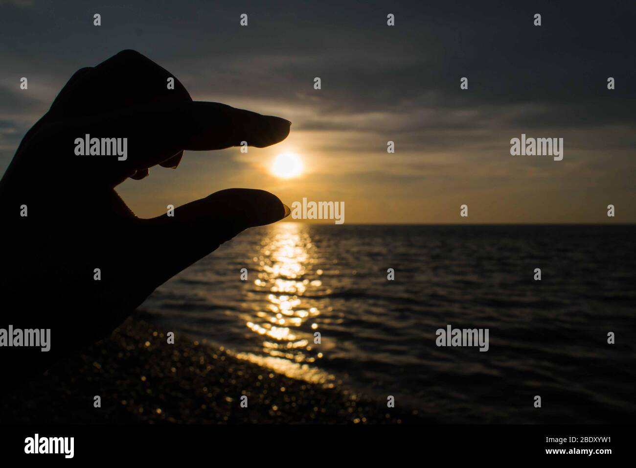 Illusion of a hand versus the size of the sun at sunset. silhoutte of ...