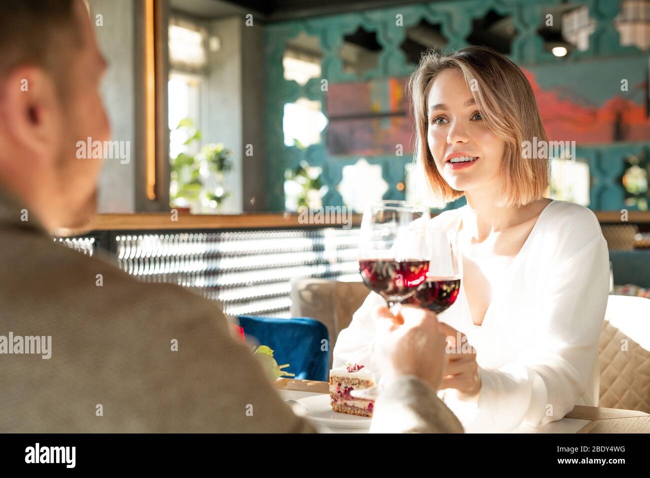 Happy young amorous woman clinking wineglass with that of her boyfriend ...