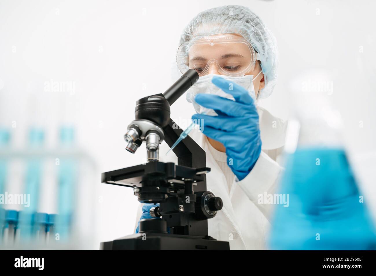 young scientist dripping liquid for coronavirus test under microscope ...