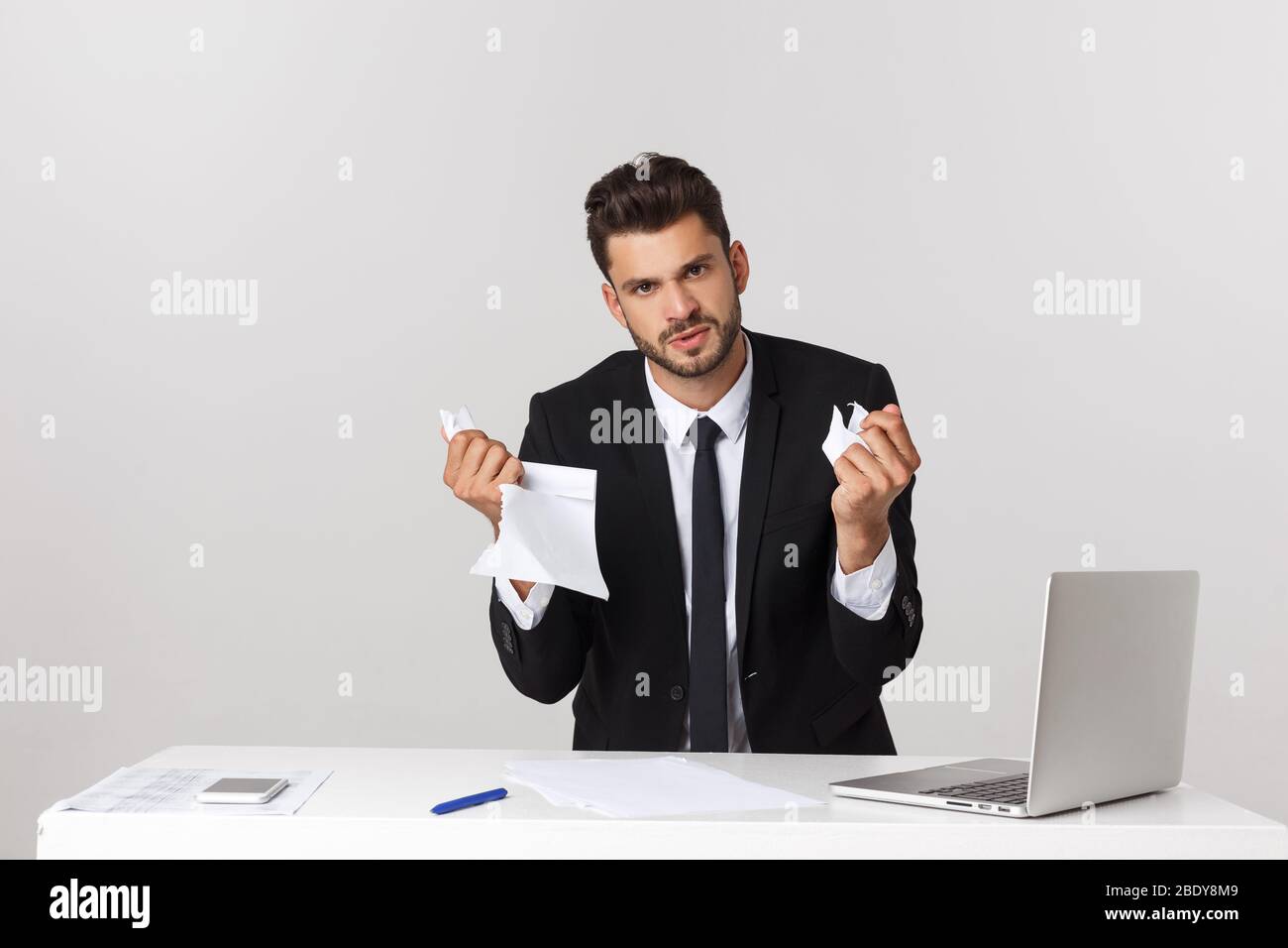 Angry young bearded man work at desk with laptop isolated over white ...