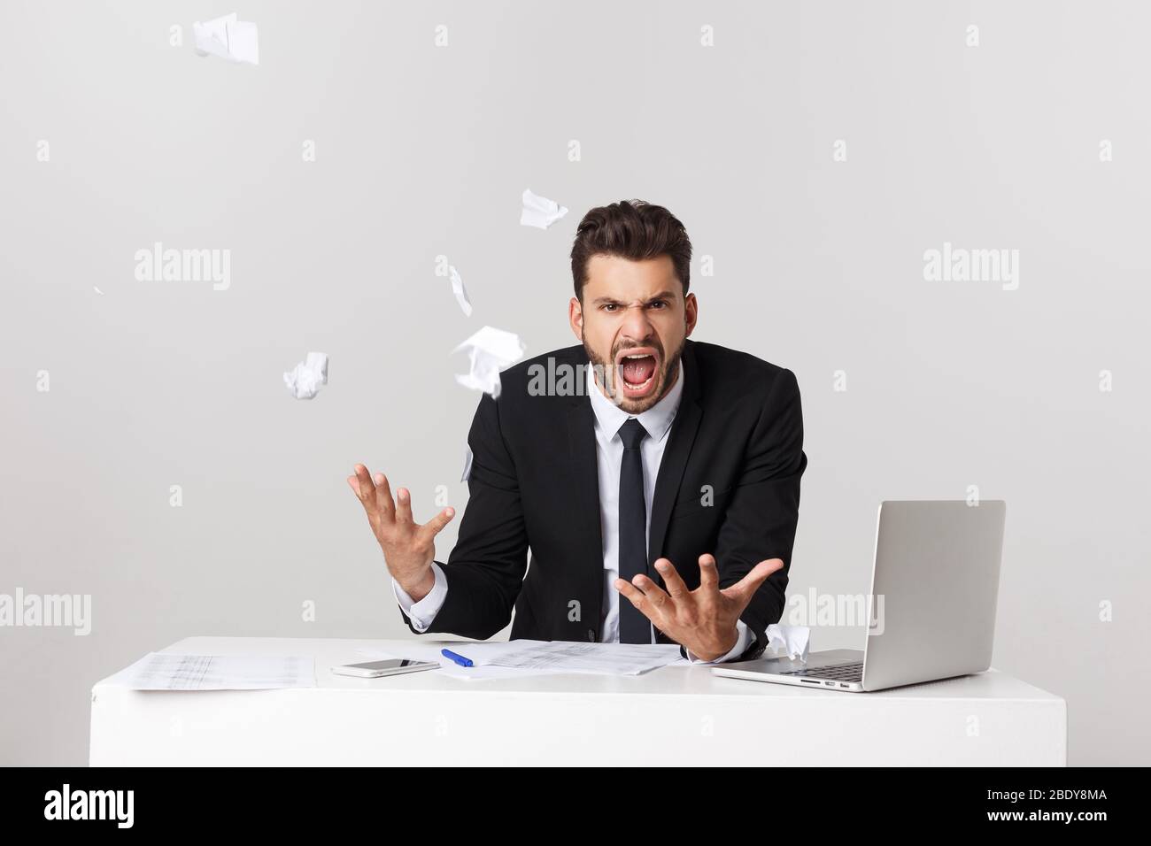 Angry young bearded man work at desk with laptop isolated over white ...