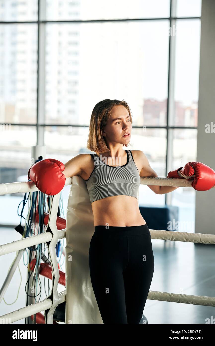 Young active female in red boxing gloves, grey crop top and black ...