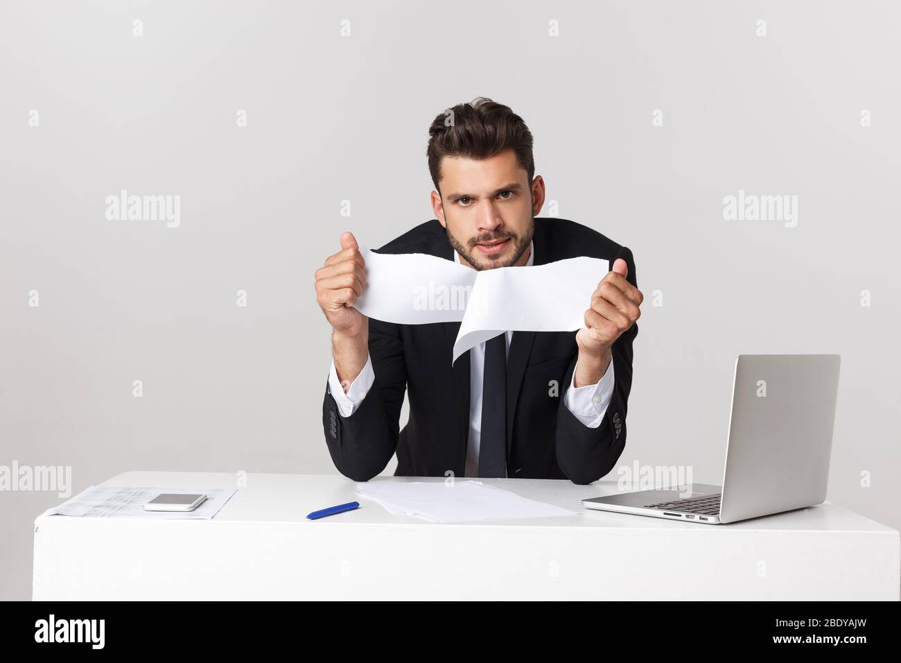 Angry young bearded man work at desk with laptop isolated over white ...