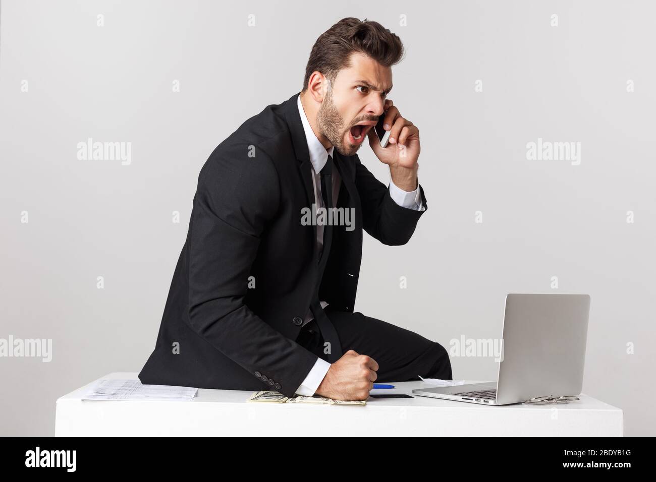 Angry businessman sitting at the table and screaming over gray ...