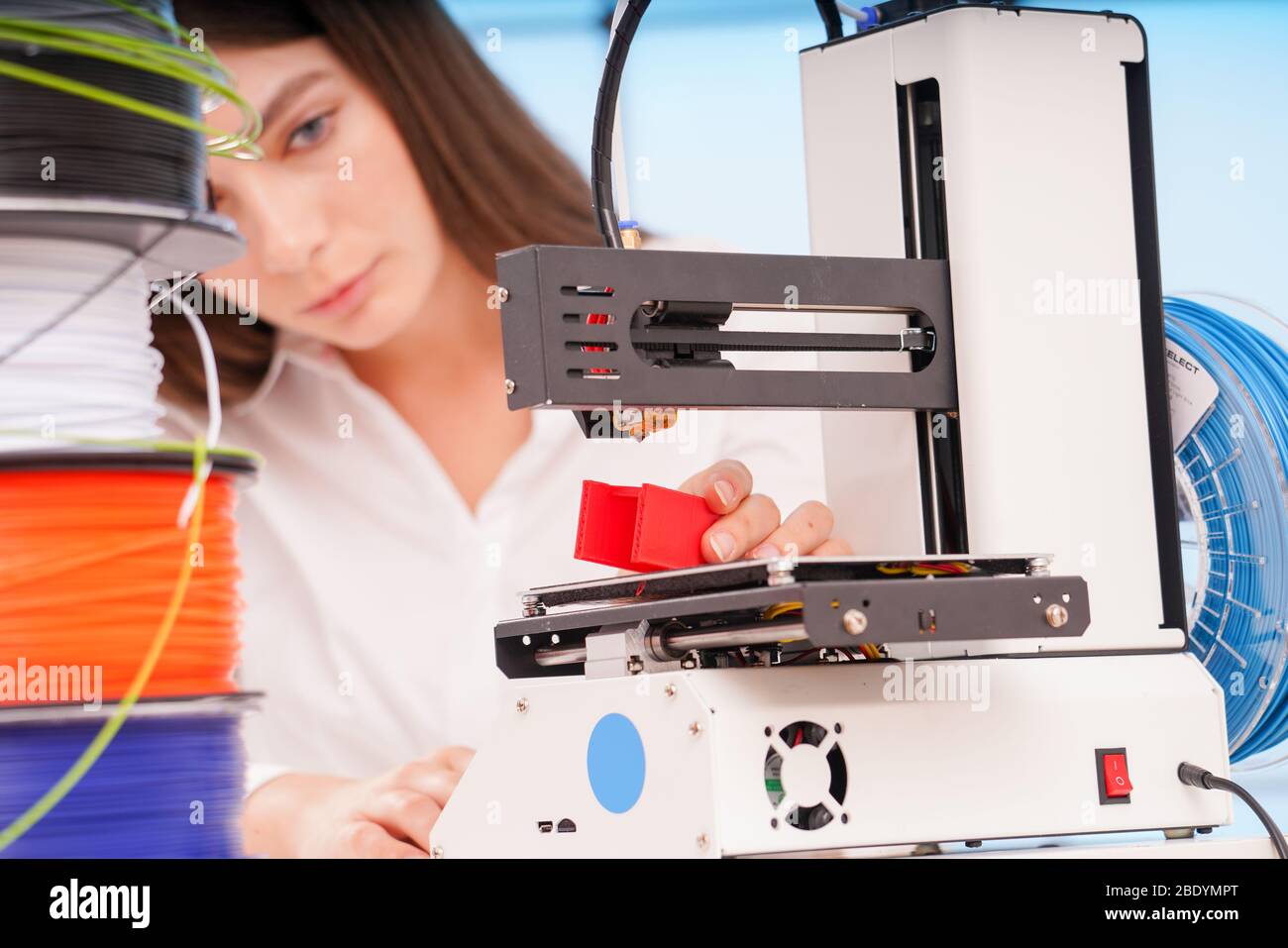 Young female designer working on a prototype device on a 3D printer ...