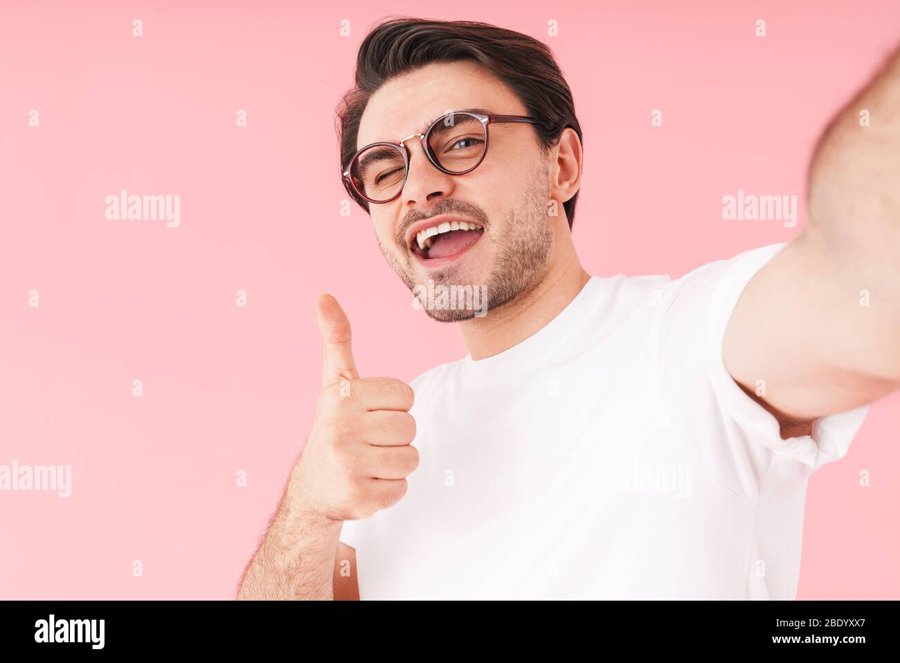 Image of caucasian joyful man wearing eyeglasses gesturing thumb up and taking selfie photo ...