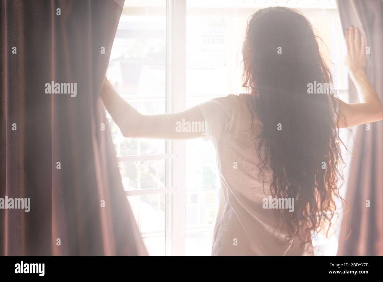 Sunny morning - a woman opens the curtains and the sun shines through ...