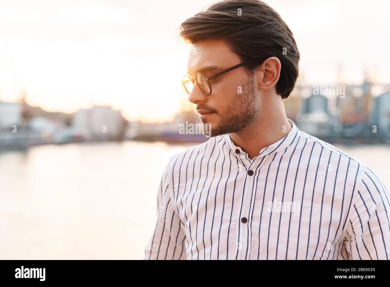 Photo of thinking young man wearing eyeglasses standing and looking ...