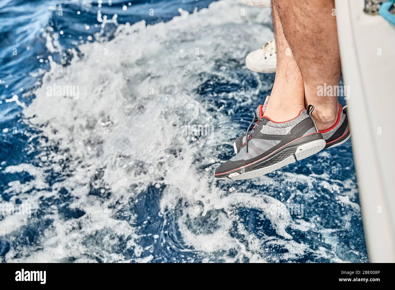 Feet of the sailor hang down from a boat board over azure water ...