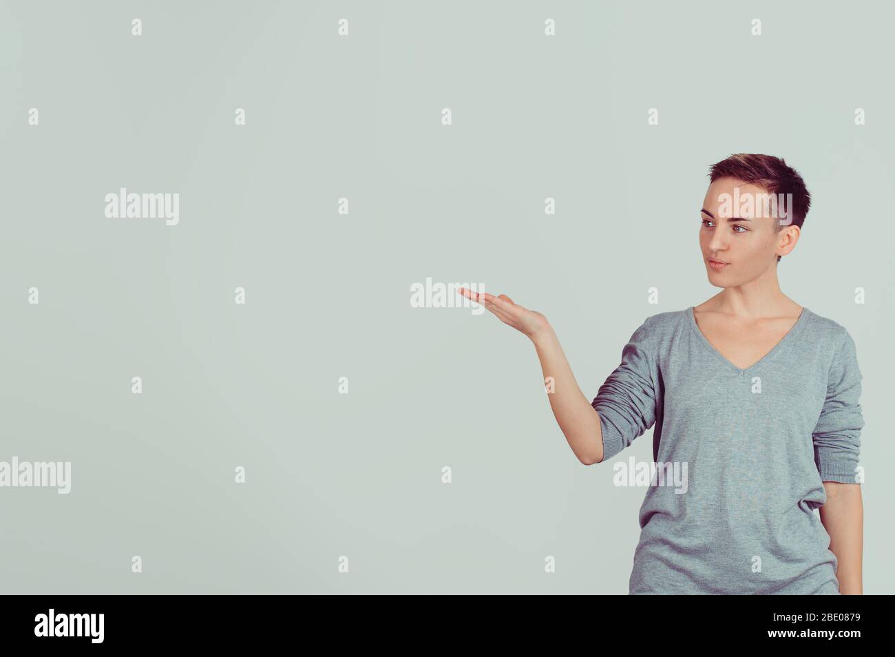 Happy smiling beautiful young woman shows a hand pointing to the side ...