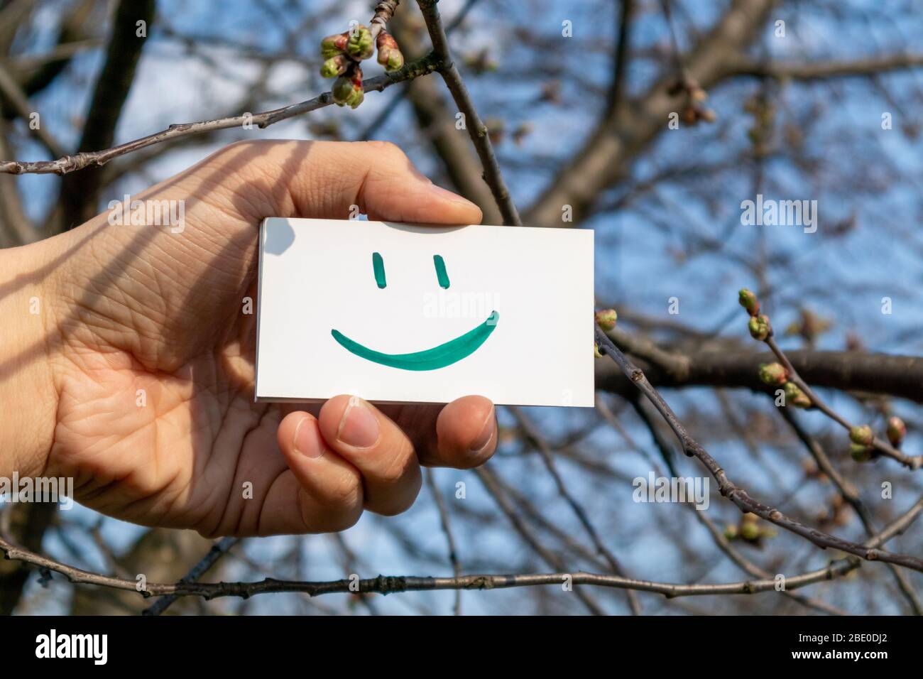 Happy green smile emoji on white paper card holding in hand on sunny ...