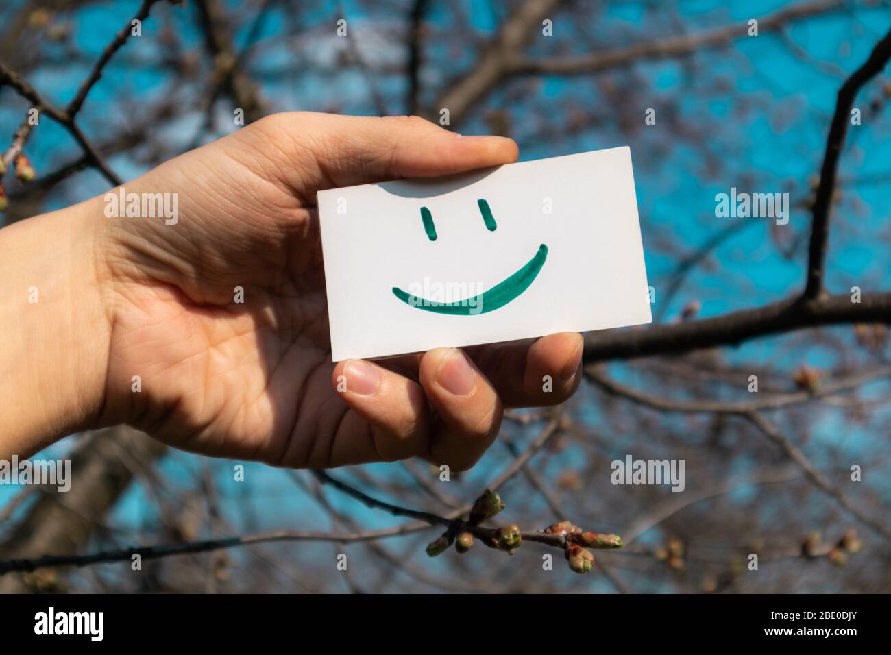 Happy green smile emoji on white paper card holding in hand on sunny ...