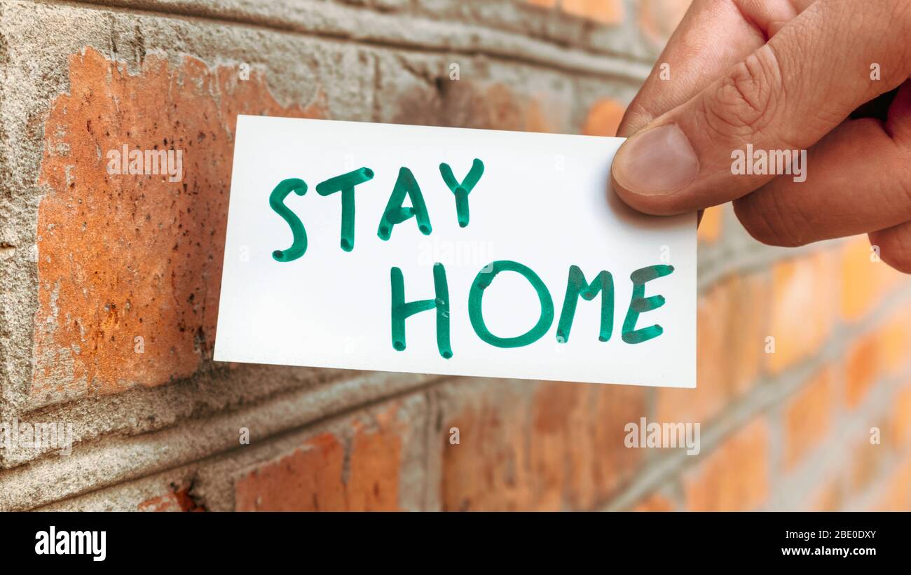 Stay home words on white card holding in hand on sunny red brick wall ...