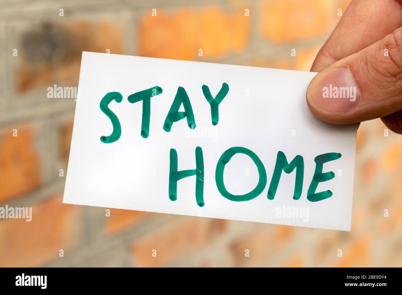 Stay home words on white card holding in hand on sunny red brick wall ...