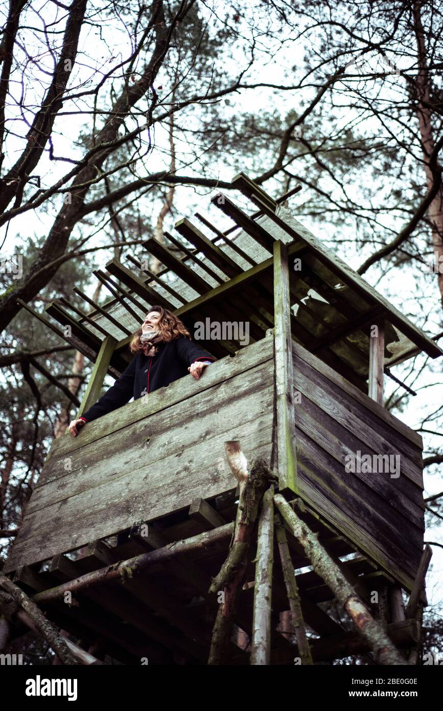 happy young woman smiles and looks out of high tree house look out ...