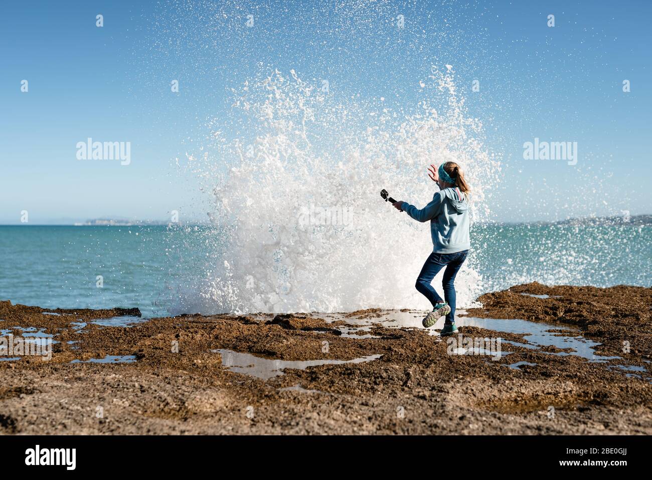 Tween startled by wave crashing over rock Stock Photo - Alamy