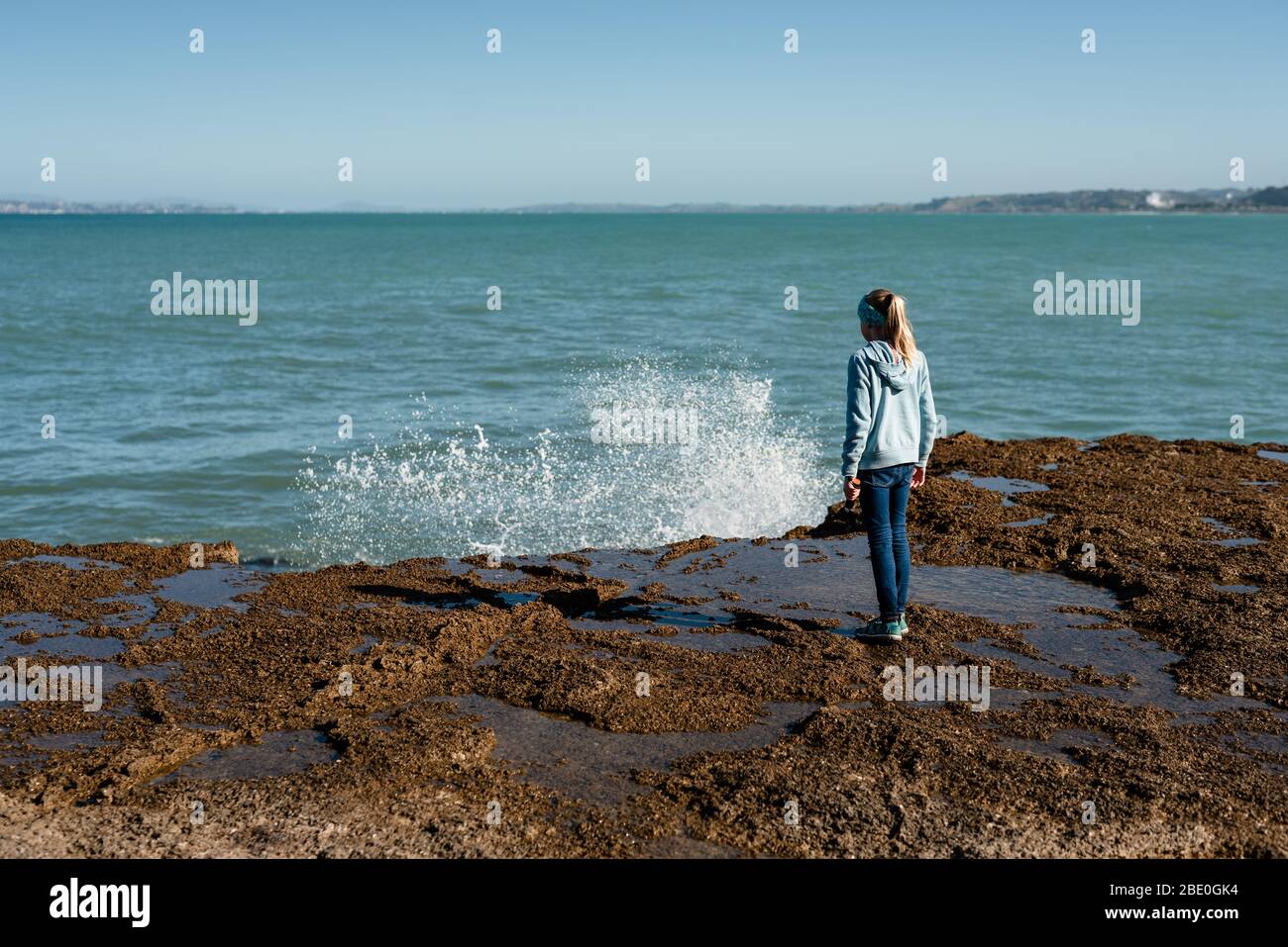Tween girl watching waves splash over rocks in New Zealand Stock Photo ...