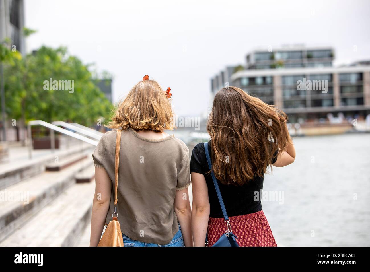 Back view of two women walking along a marina. One is flipping her hair ...