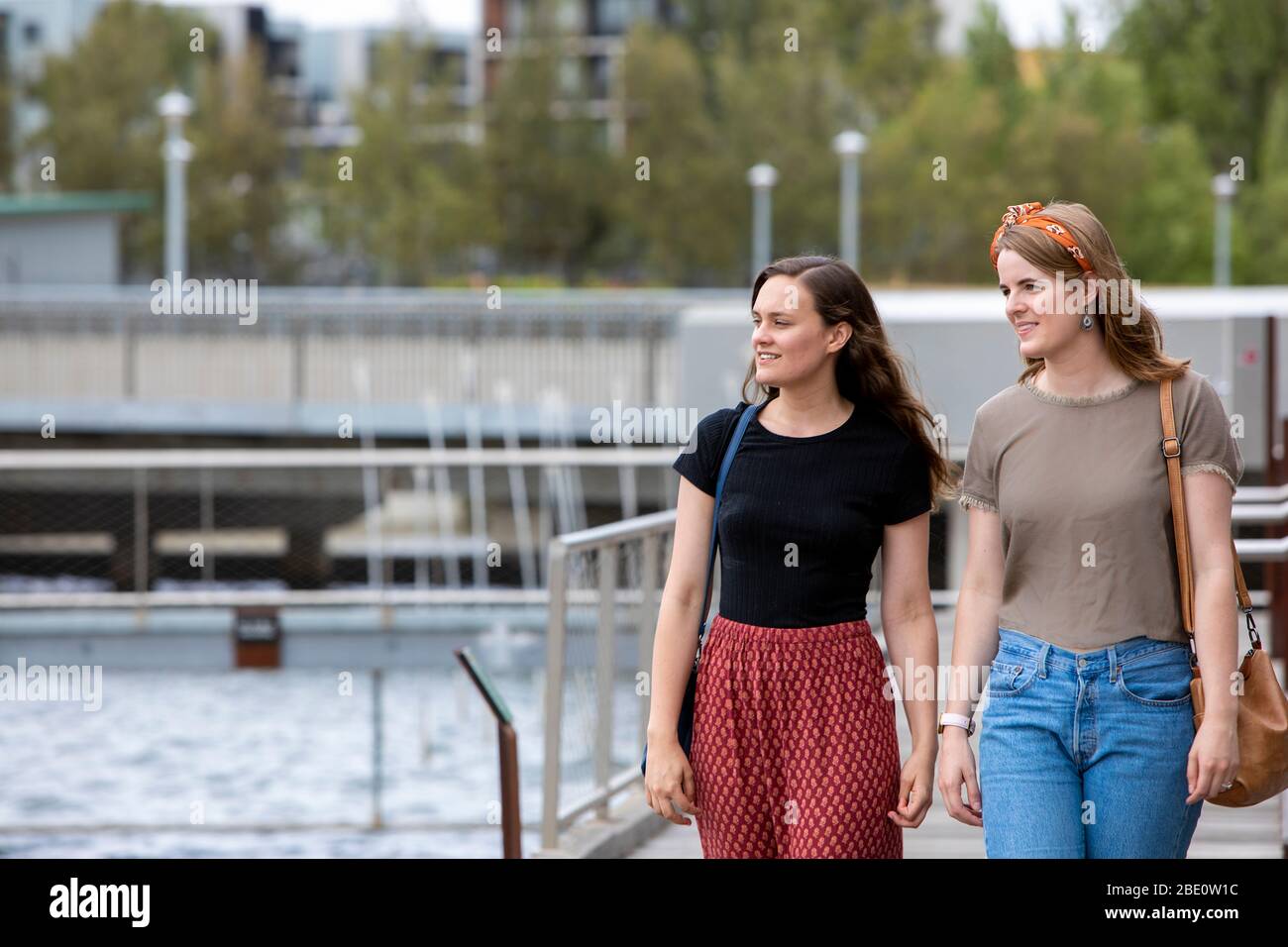 Two young women walking along a marina looking left Stock Photo - Alamy