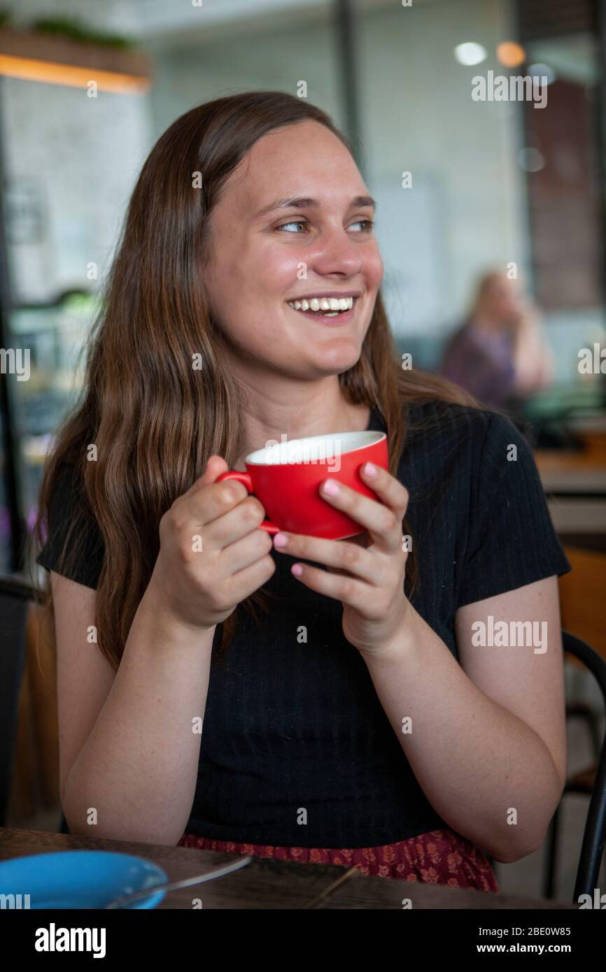 Young female adult in coffee shop with girlfriend chatting and drinking ...