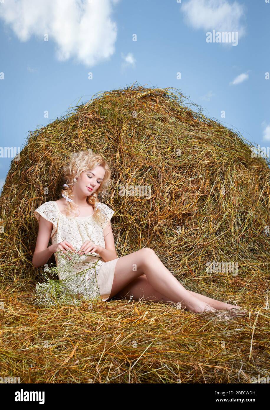 portrait of beautiful blonde country girl sittitng on yellow hay with ...