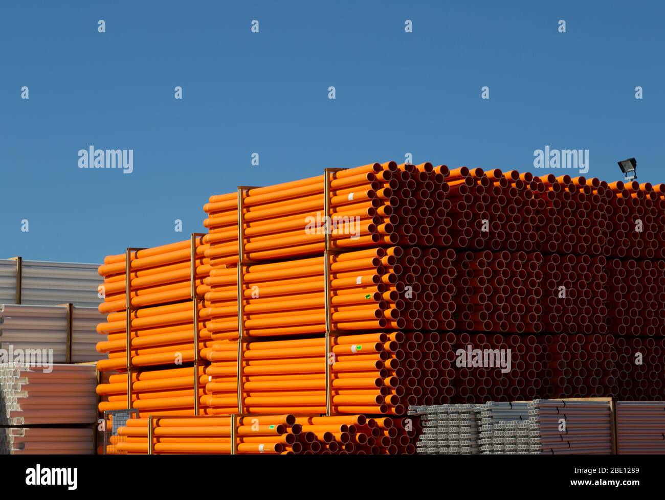 Orange and white plastic pipes stacked in an industrial storage yard ...