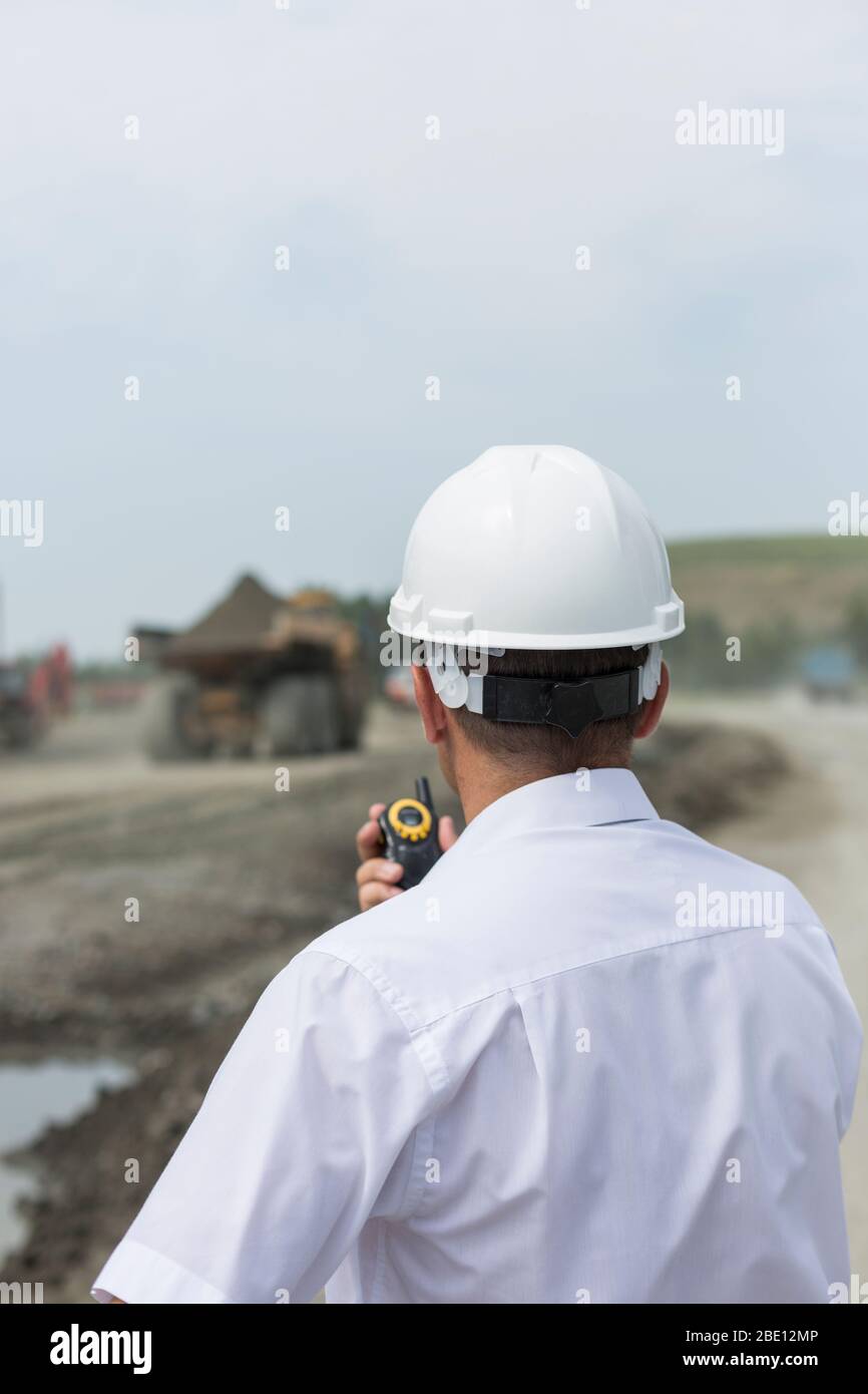 Mining engineer in white shirt and helmet supervises driving dumpers in ...
