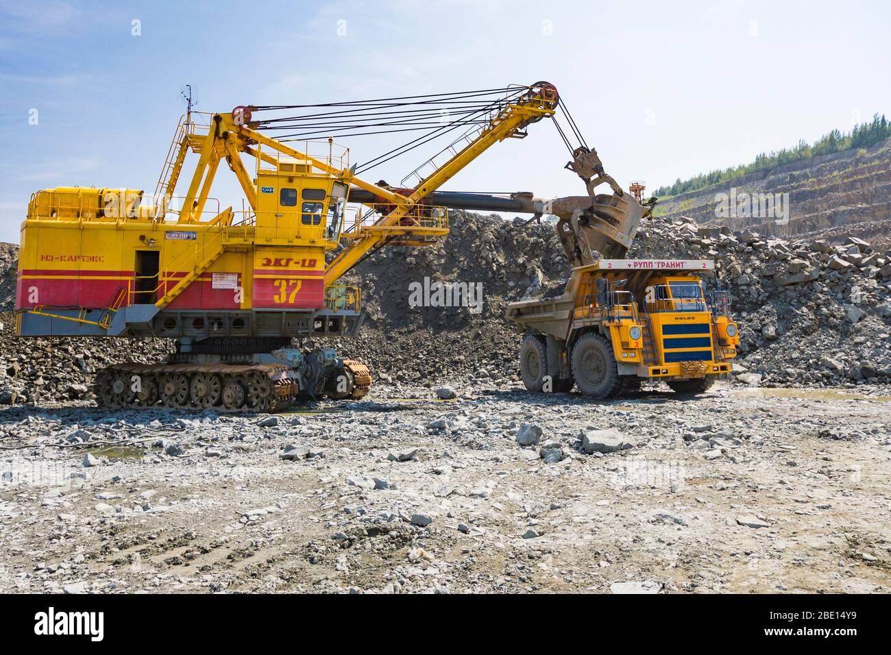 A mining excavator loads a huge truck with granite rock Stock Photo - Alamy
